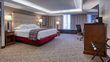 Quarto de hotel com uma cama grande, uma escrivaninha, uma cadeira e uma luminária de mesa.