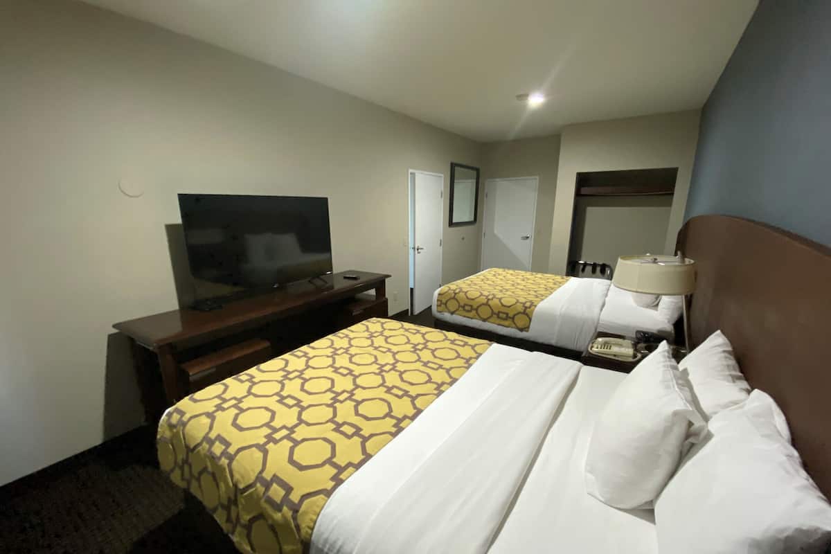 Quarto de hotel com duas camas, televisão, escrivaninha e espelho.