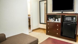 Quarto de hotel compacto com sofá, mesa pequena, TV, micro-ondas e mini-geladeira.