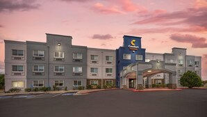 Um hotel com design moderno, exibindo uma placa grande da 'Comfort Suites', vários andares e um estacionamento.