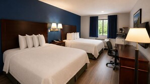 Quarto de hotel com duas camas, uma escrivaninha, uma cadeira, micro-ondas e televisão.