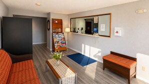 Quarto com sofá, um banco, mesa com vaso, espelho, um mural e área de recepção com sinalização.