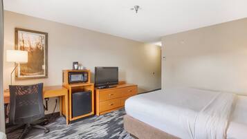 Quarto de hotel com uma cama, uma escrivaninha com computador, televisão e um pequeno frigorífico.