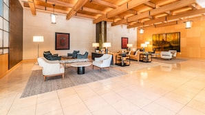 Um hall espaçoso com teto alto, vigas de madeira e móveis modernos. Há vários espaços de estar com luminárias e obras de arte nas paredes.
