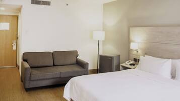 Quarto de hotel com cama, sofá, mesa de cabeceira com luminária e telefone.