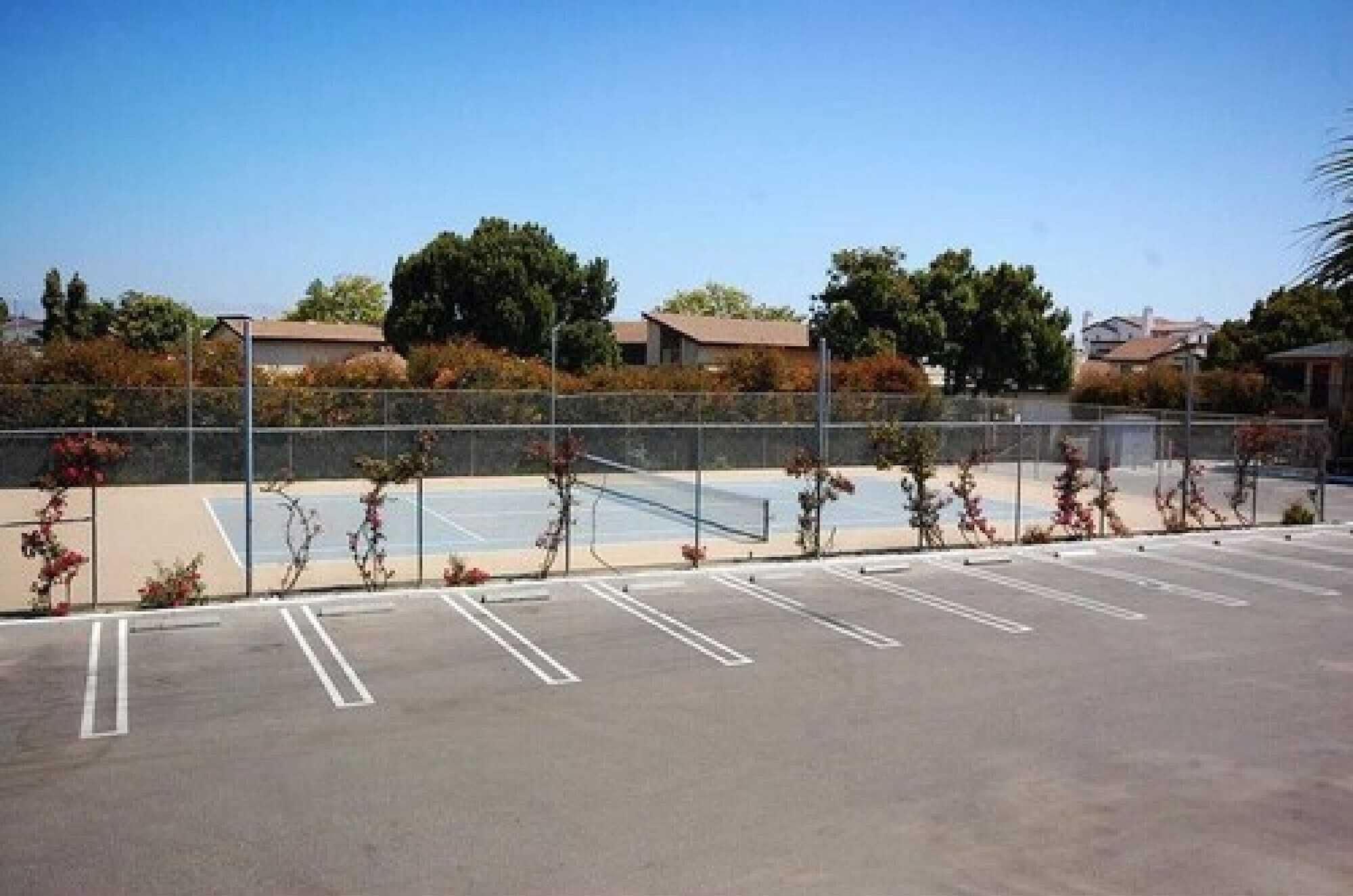 Um estacionamento com vagas demarcadas, cerca e árvores ao fundo.