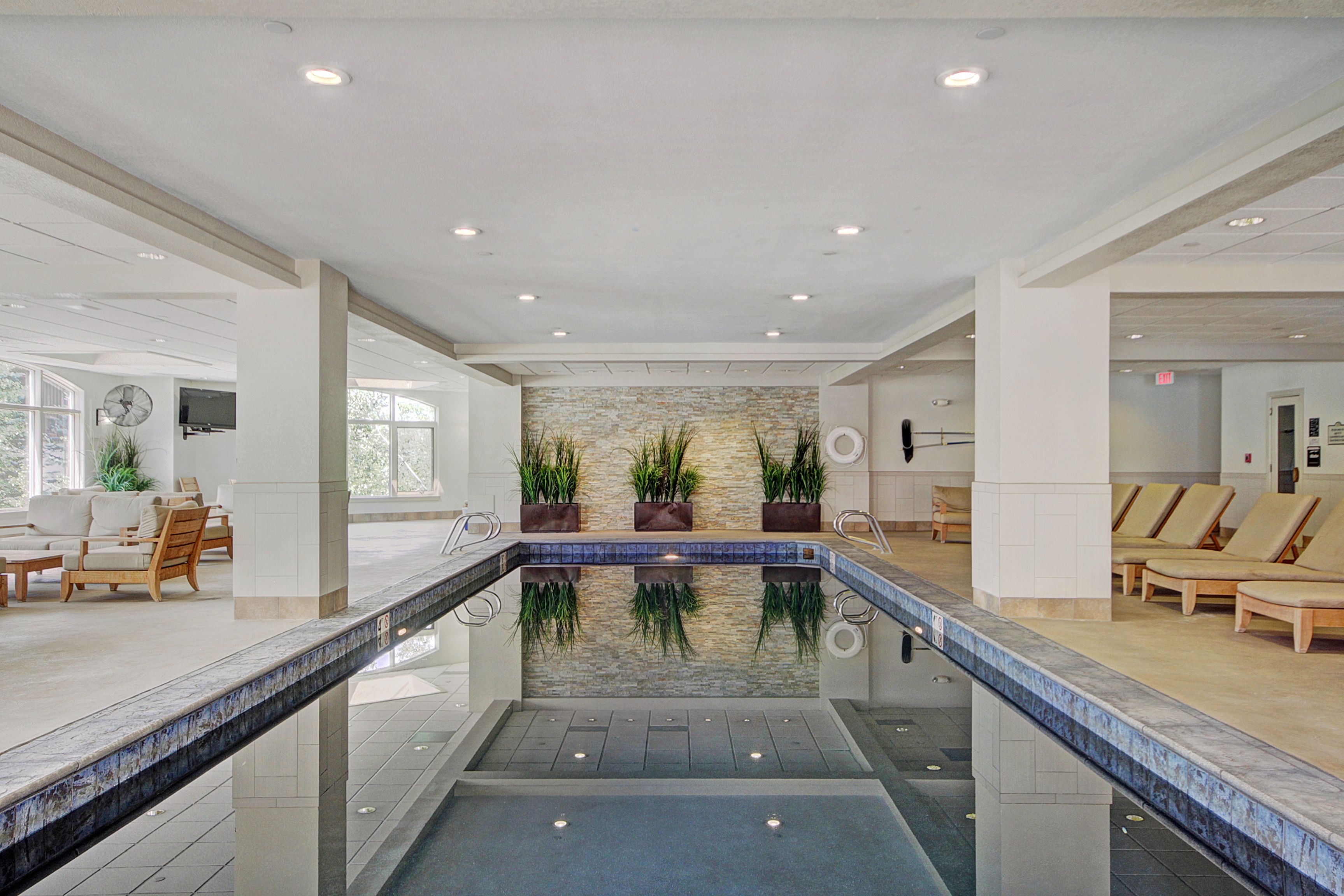 Piscina com muro de pedra e plantas ao fundo, rodeada por espreguiçadeiras e um espaço de estar.