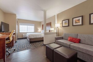 Quarto de hotel com cama, escrivaninha com cadeira, sofá e televisão.