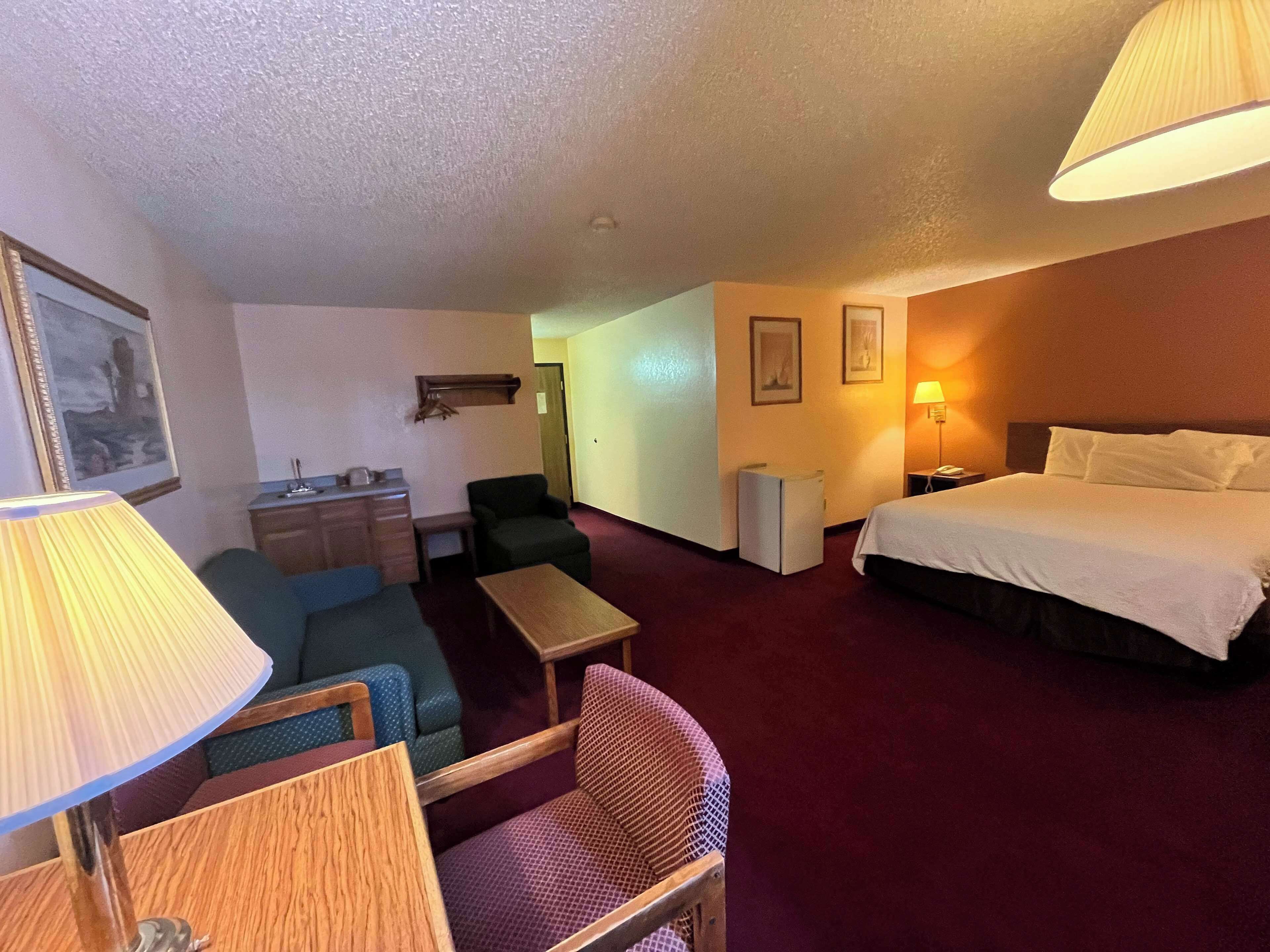 Quarto de hotel com cama, escrivaninha, cadeira, mesinha e abajur.