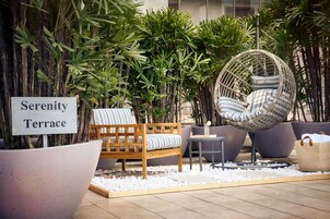 Um Serenity Terrace com um banco de madeira, uma cadeira de vime e plantas em vasos.