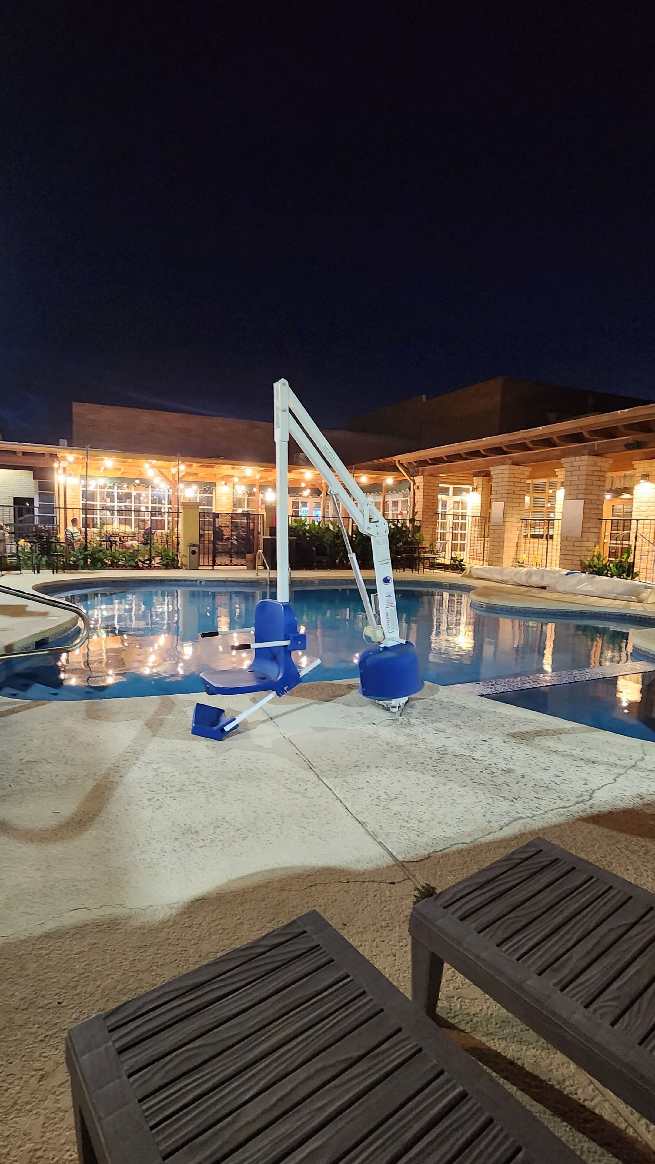 Piscina com espreguiçadeiras, elevador de piscina e um edifício iluminado ao fundo.