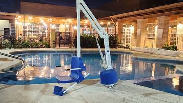 Piscina com espreguiçadeiras, elevador de piscina e um edifício iluminado ao fundo.