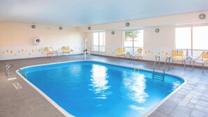 Uma piscina interior com água azul cristalina, rodeada por cadeiras amarelas e brancas, e grandes janelas que permitem a entrada de luz natural.