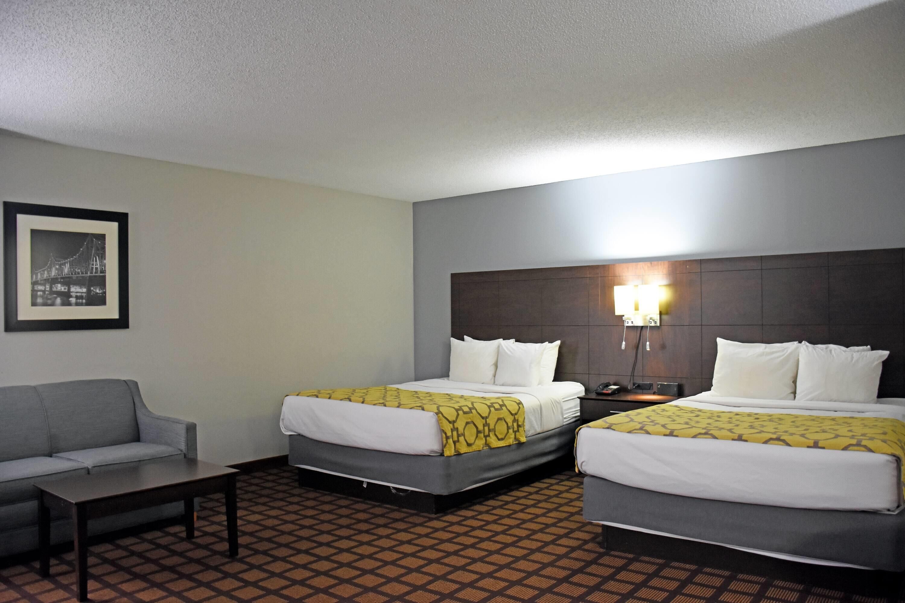 Quarto de hotel com duas camas, um sofá, uma mesa de cabeceira e um quadro na parede.