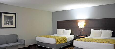 Quarto de hotel com duas camas, um sofá, uma mesa de cabeceira e um quadro na parede.