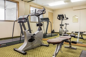 Uma academia com diversos equipamentos de exercícios, incluindo esteiras, elípticos e um banco.
