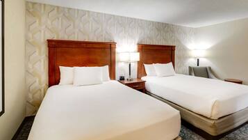 Quarto de hotel com duas camas, cabeceiras de madeira, mesas de cabeceira com abajures e papel de parede estampado.