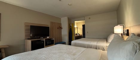 Quarto de hotel com duas camas, televisão, escrivaninha e espelho.