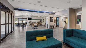 Um hall amplo com sofás verde-água, espaço para refeições e um balcão de recepção.