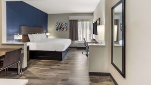 Quarto de hotel com cama, escrivaninha, cadeira e um espelho grande.