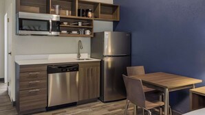 Uma cozinha moderna com micro-ondas embutido, geladeira de aço inoxidável, armários de madeira e um espaço de jantar com mesa e cadeiras.