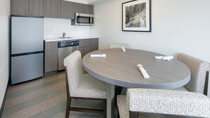 Uma cozinha compacta com eletrodomésticos modernos, uma mesa de jantar com quatro cadeiras e um quadro na parede.