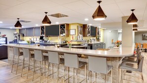 Uma área de bar moderna com um balcão comprido, banquetas e iluminação pendente.