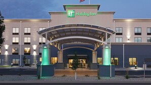 Entrada de um hotel Holiday Inn com galeria coberta, bandeira americana e pilares iluminados.