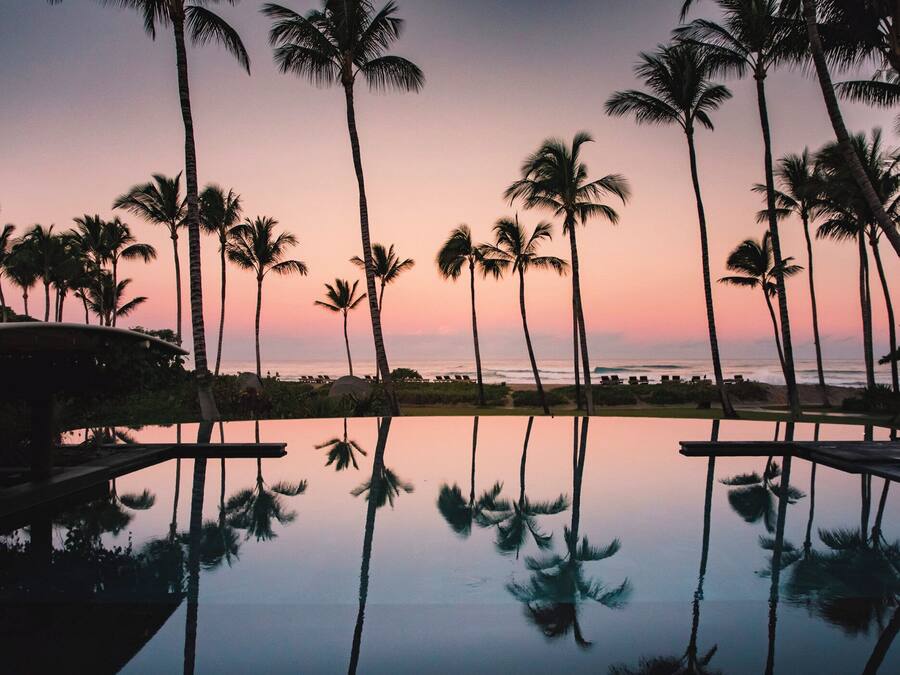 Uma área de piscina tranquila com palmeiras e vista para o pôr do sol.