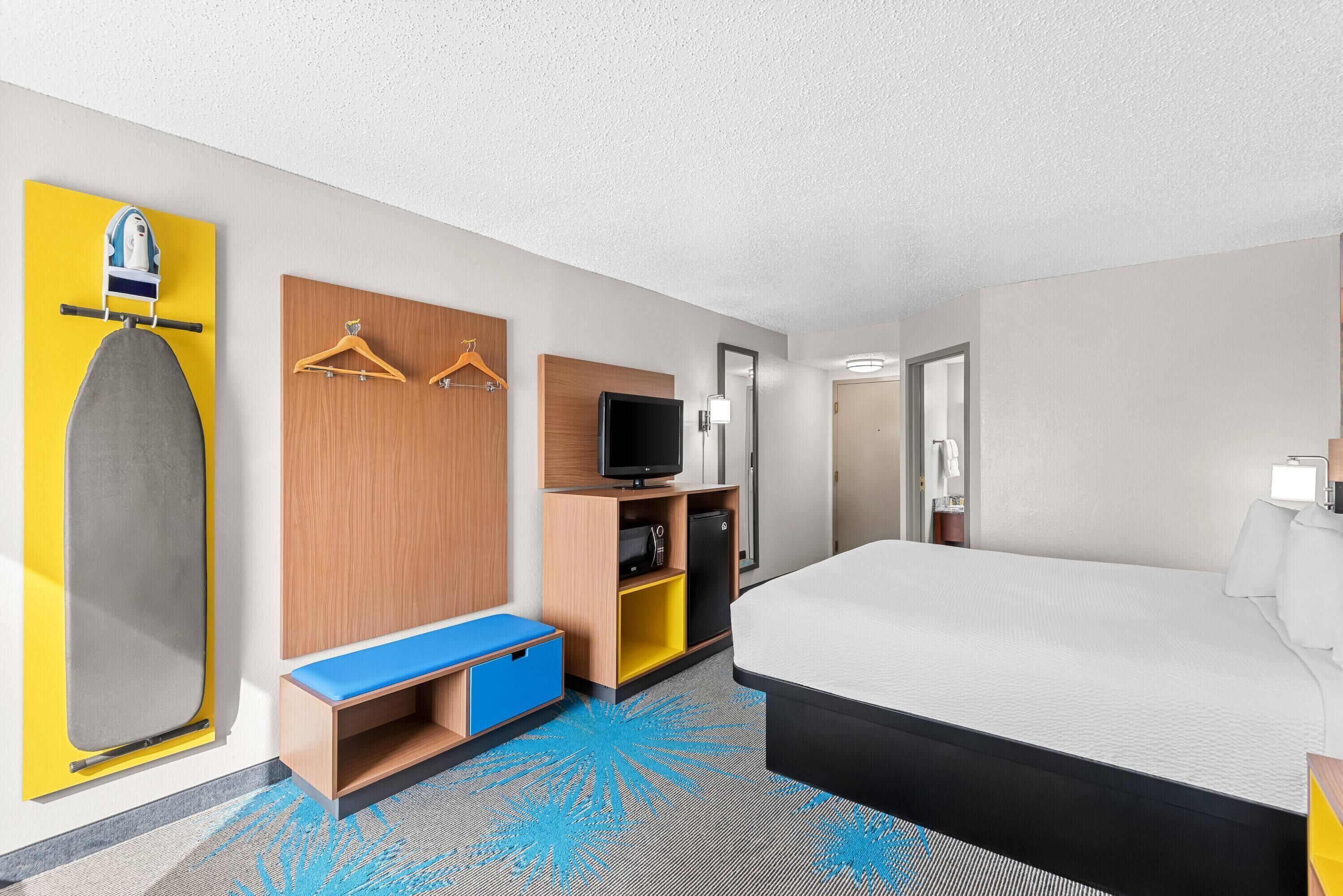 Quarto de hotel com cama, um banco, televisão e guarda-roupa.