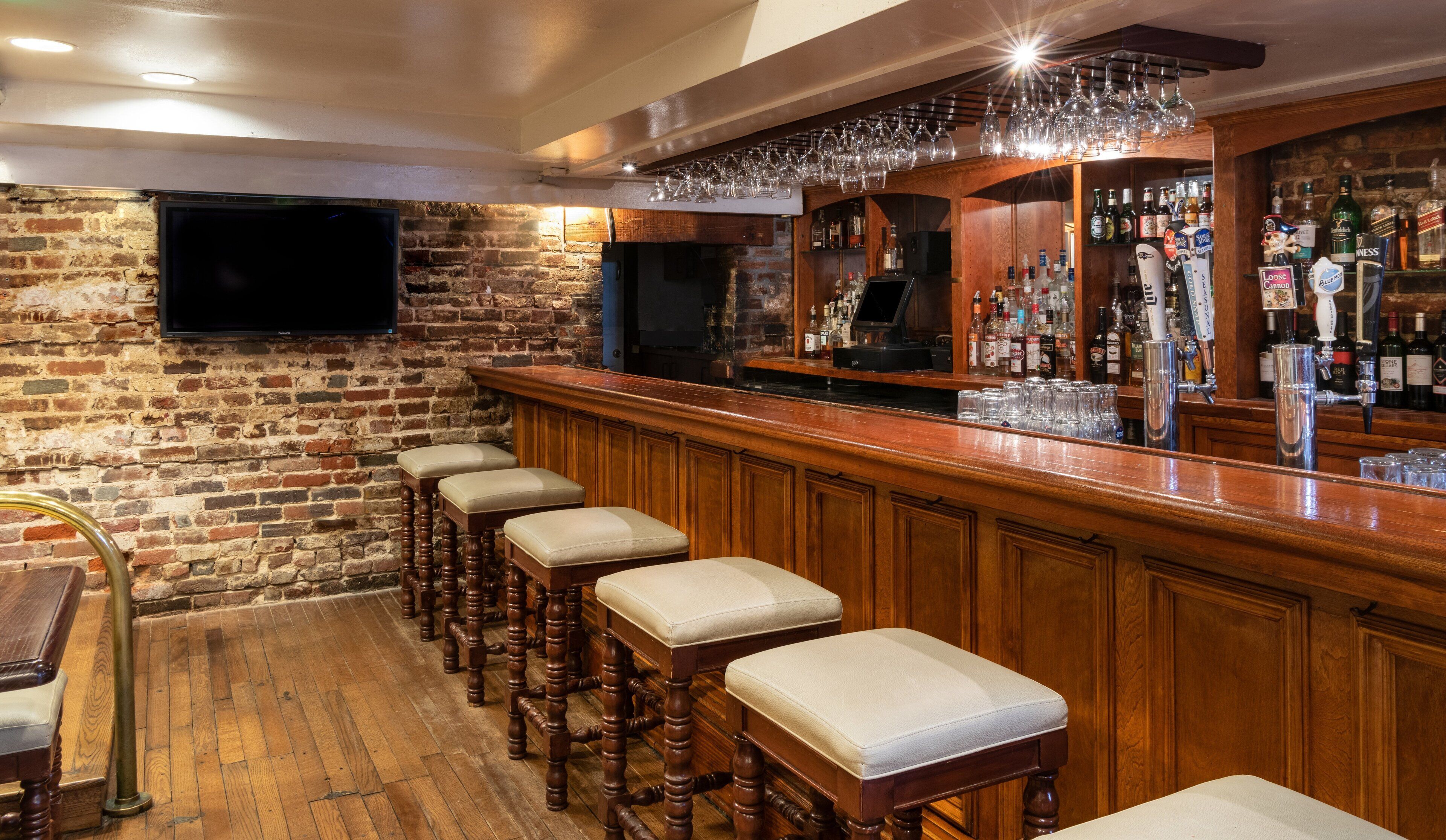 Uma área de bar com bancos de madeira, parede de tijolos e televisão sobre a lareira.