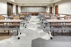 Sala de conferência com mesas, cadeiras e garrafas de água.