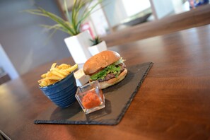 Uma mesa de jantar com um hambúrguer e batatas fritas em um prato de ardósia preta.