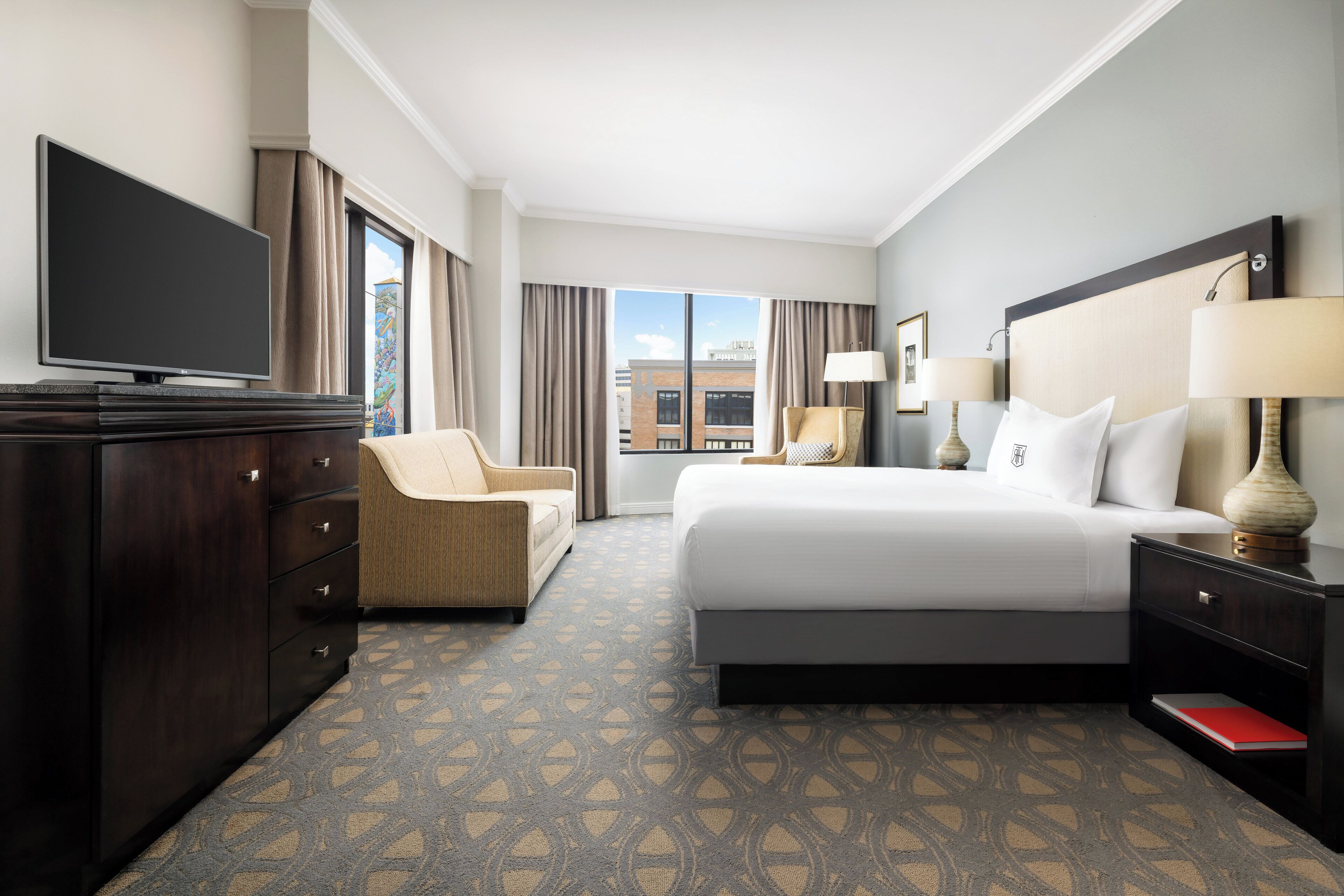 Quarto de hotel com uma cama grande, televisão, escrivaninha, cadeira e vista para a cidade pela janela.