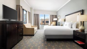 Quarto de hotel com uma cama grande, televisão, escrivaninha, cadeira e vista para a cidade pela janela.
