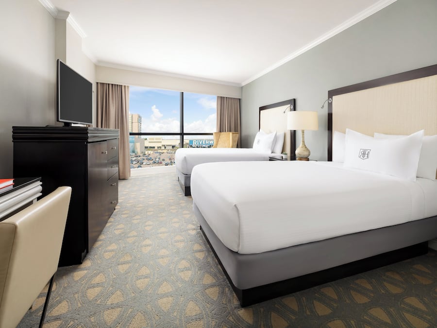 Quarto de hotel com duas camas, uma escrivaninha, televisão e vista para a cidade.
