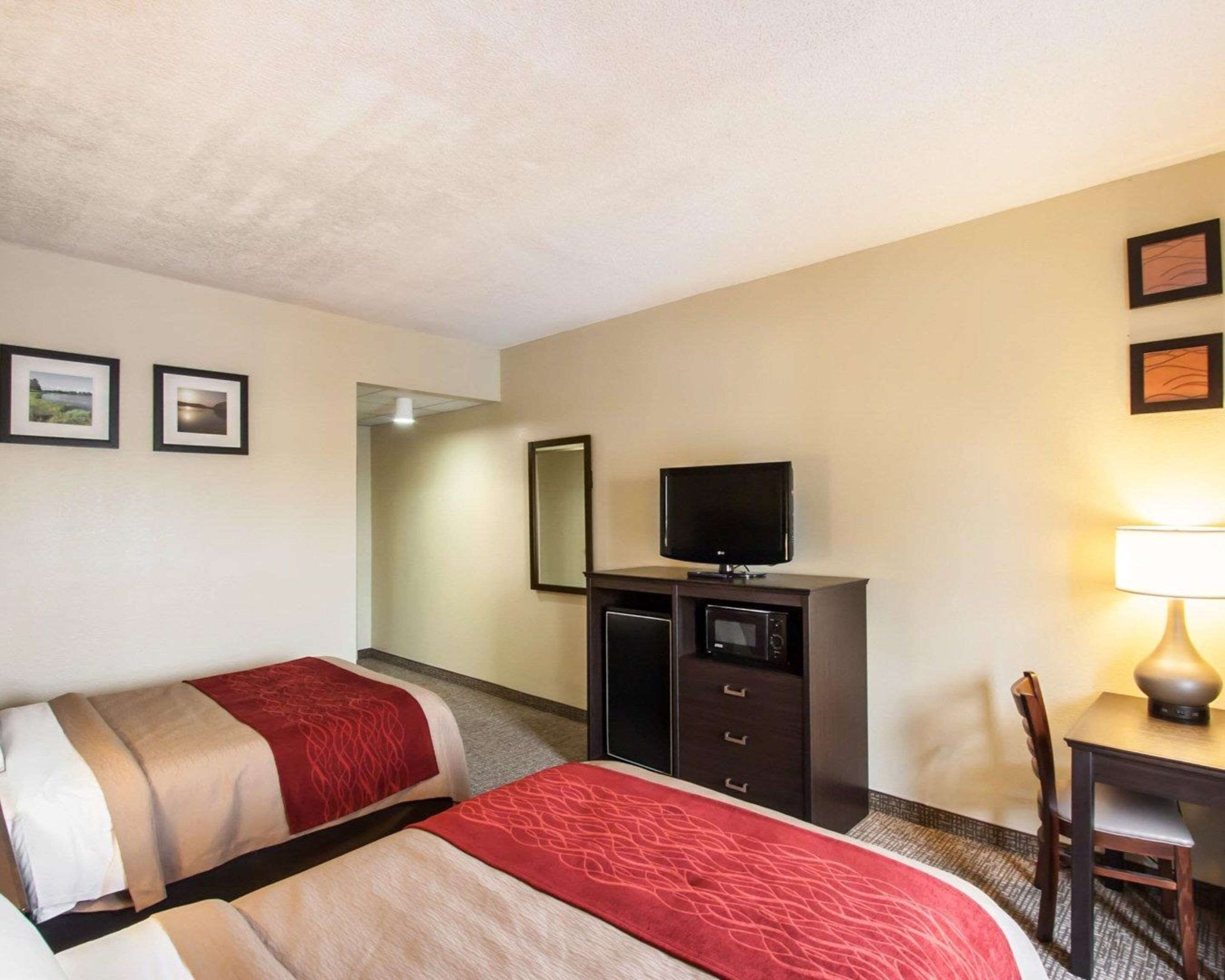 Quarto de hotel com duas camas, televisão, escrivaninha com luminária e espelho.
