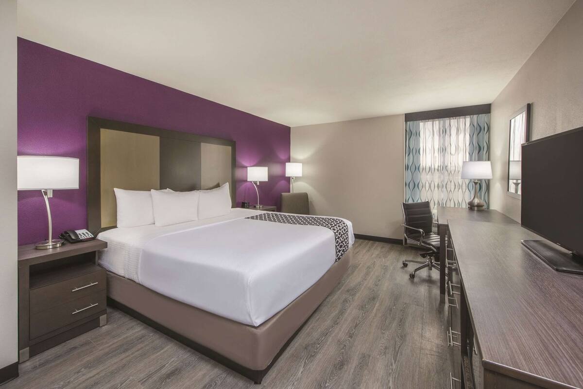 Quarto de hotel com uma cama grande, mesas de cabeceira, escrivaninha e televisão.