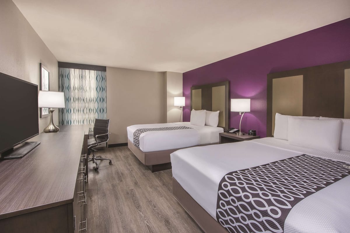 Quarto de hotel com duas camas, uma escrivaninha e uma janela grande com vista.