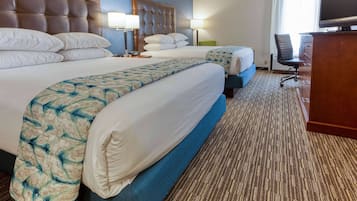 Quarto de hotel com duas camas, uma cabeceira grande, uma escrivaninha com cadeira e uma televisão.