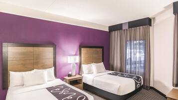 Quarto de hotel com duas camas, uma mesa de cabeceira com abajur e uma janela com cortinas.