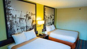 Quarto de hotel com duas camas, uma mesa de cabeceira com abajur e uma grande moldura na parede.