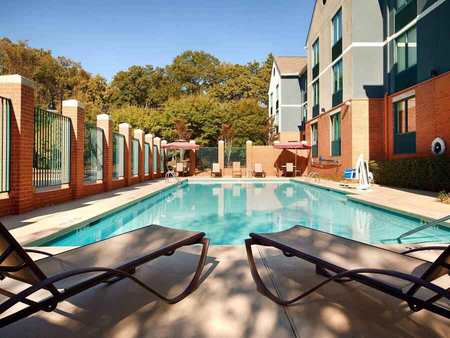 Piscina com espreguiçadeiras e um prédio de tijolos ao fundo.