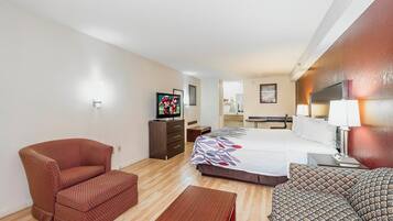 Quarto de hotel com cama, televisão, cadeira, escrivaninha e abajur.