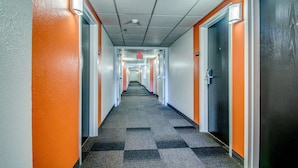 Corredor de hotel com pisos carpetados, paredes alaranjadas e portas em ambos os lados.