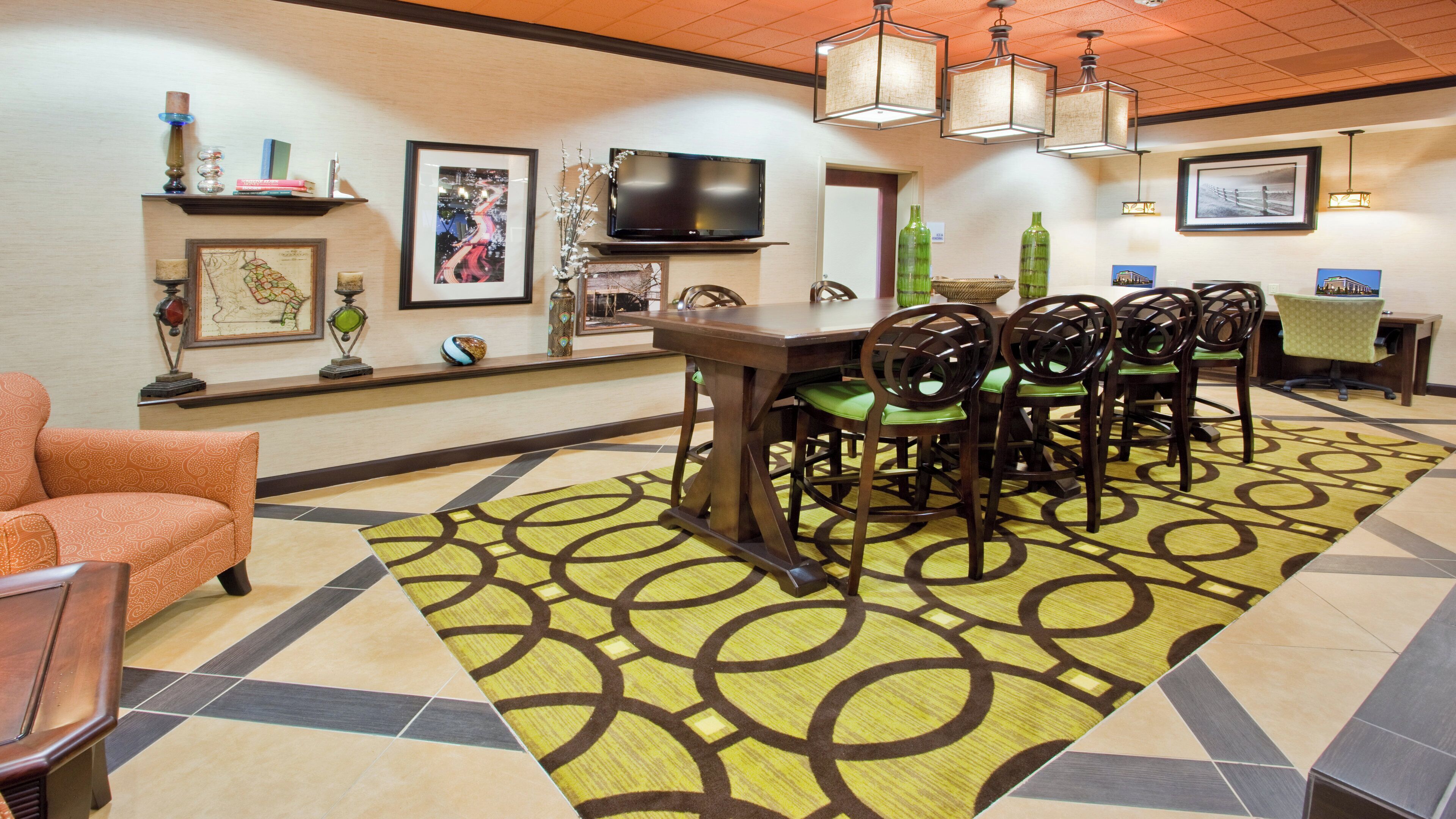 Uma área de refeições com mesa e cadeiras, uma televisão na parede e diversos objetos decorativos em prateleiras.