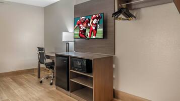 Quarto moderno com televisão de tela plana na parede, uma escrivaninha com cadeira e micro-ondas embutido nos armários.