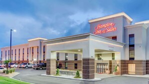 Um Hampton Inn & Suites com fachada moderna, entrada coberta e estacionamento.