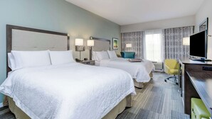Quarto de hotel com duas camas, uma mesa de escritório com um computador, uma cadeira e uma televisão.