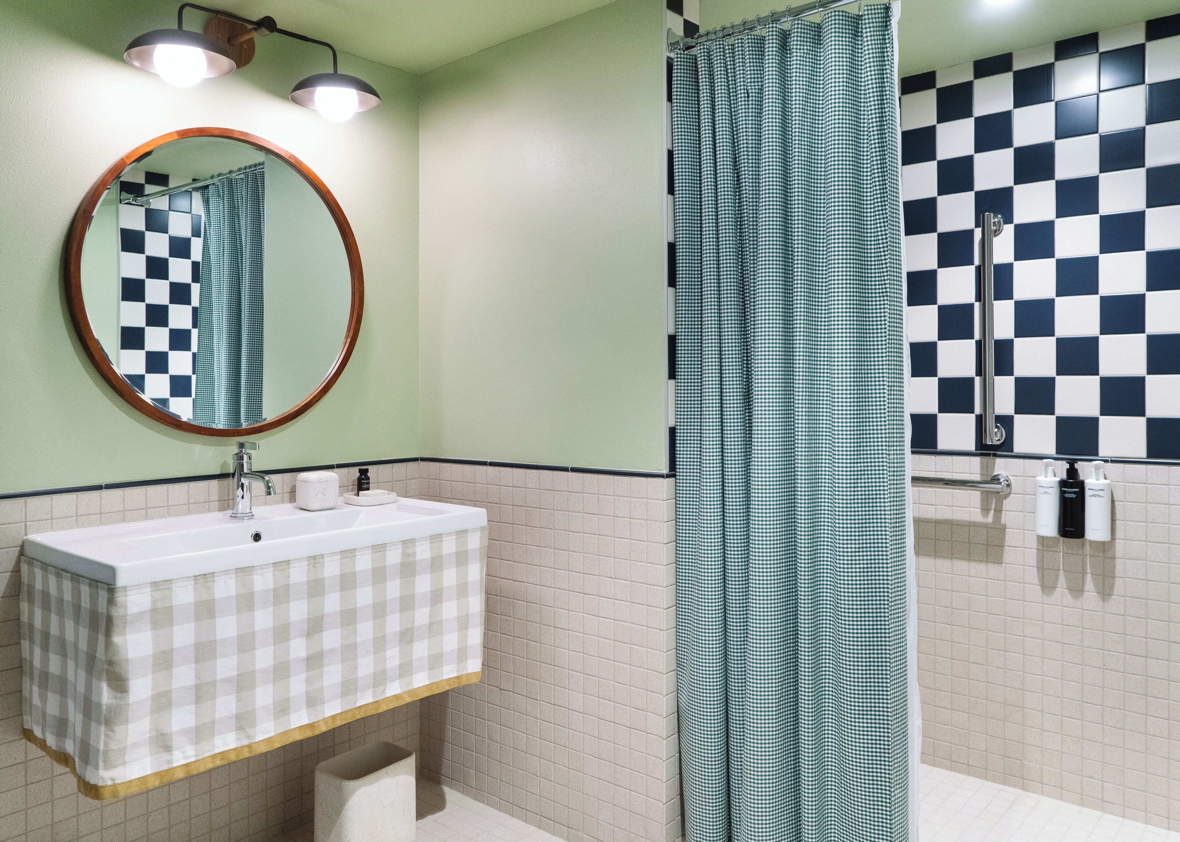 Um banheiro com pia quadriculada, espelho, cortina de chuveiro e parede revestida de azulejos.